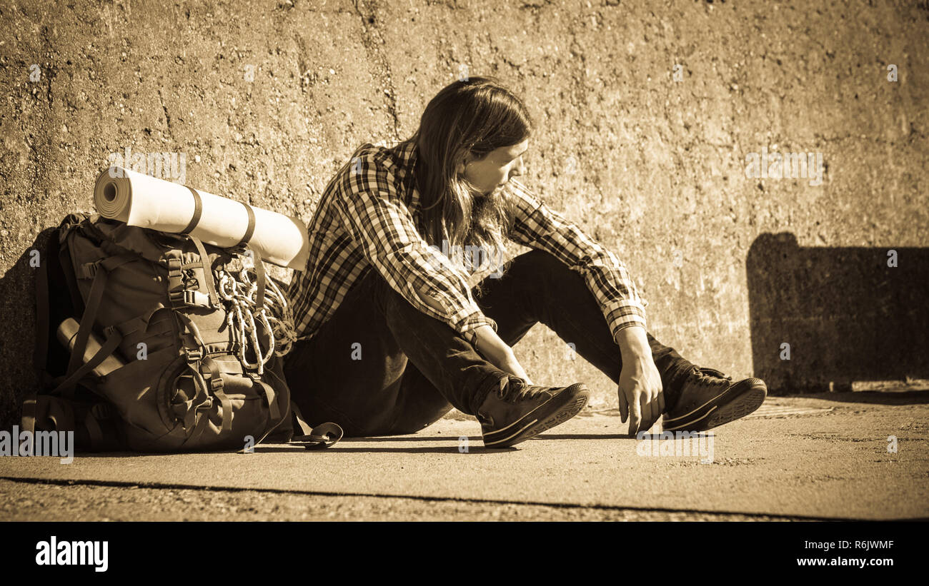 Man tourist backpacker relaxing outdoor sitting tired by grunge wall ...