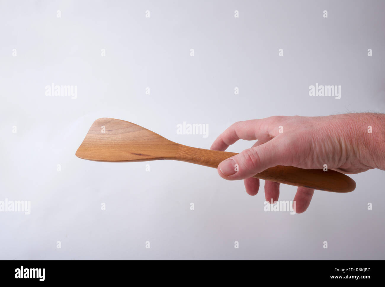 A male hand reaches to grasp a handmade wooden spatula, against a white ...