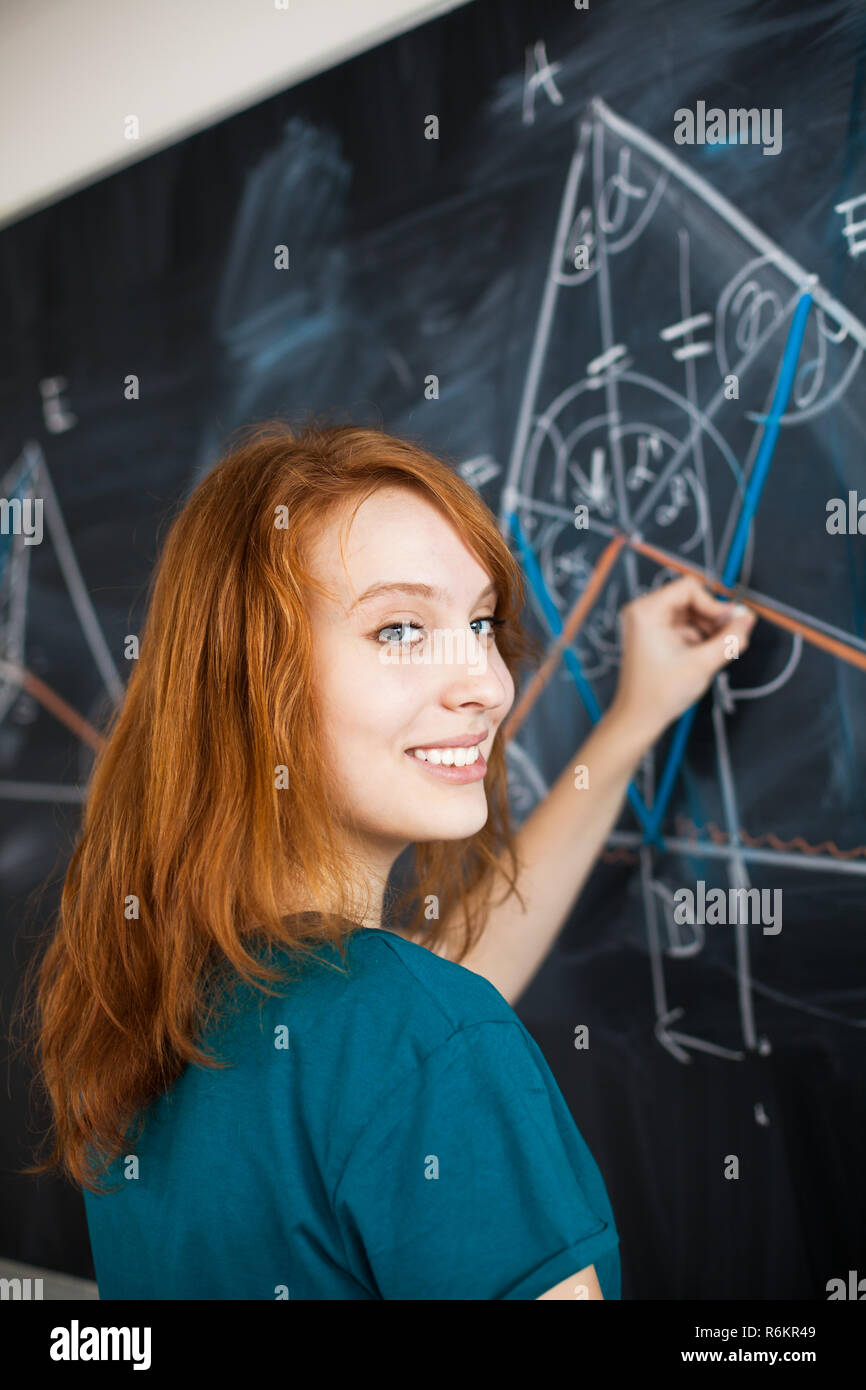Portrait of a pretty young college student writing on the blackboard ...