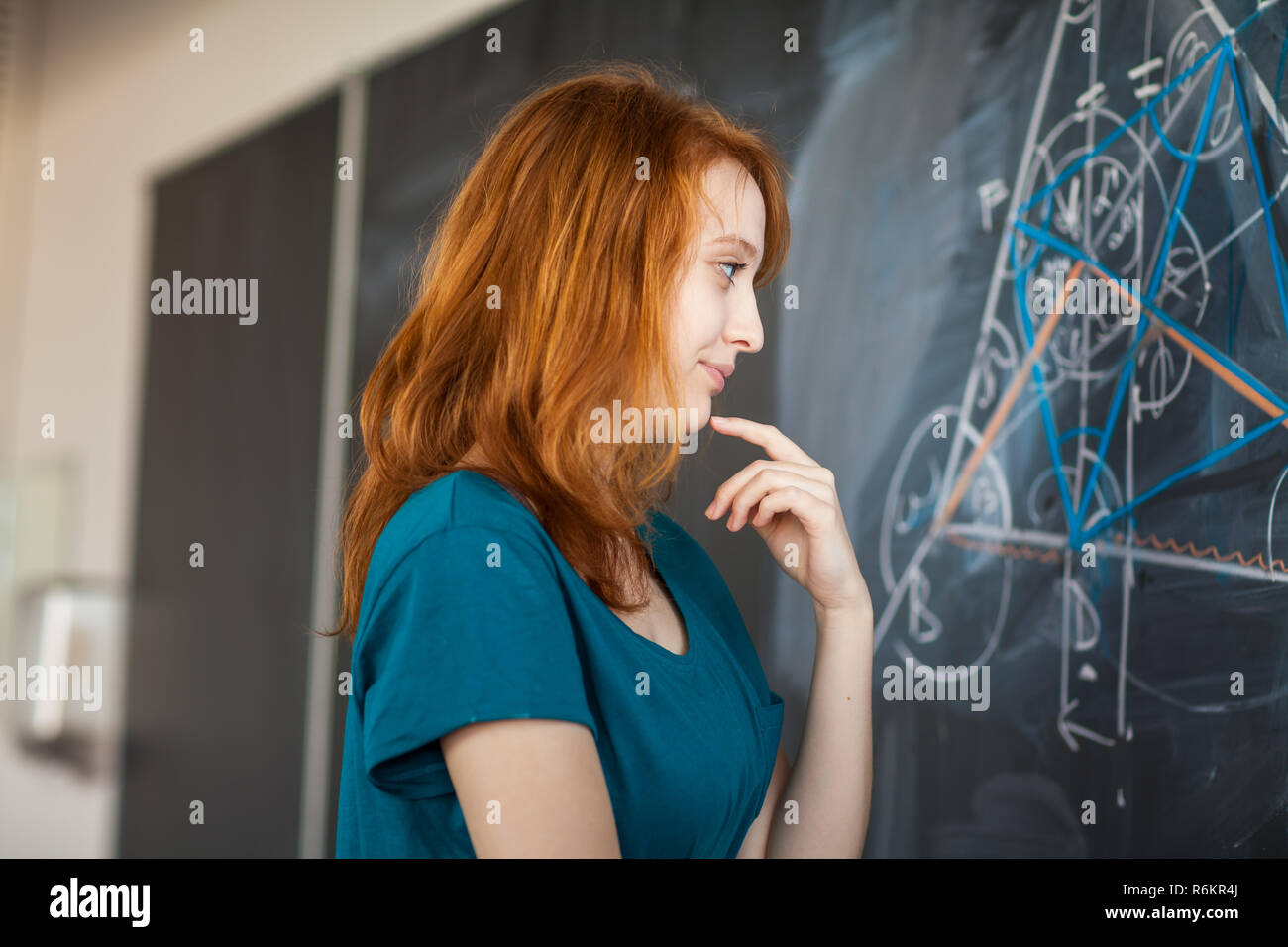 Portrait of a pretty young college student writing on the blackboard ...