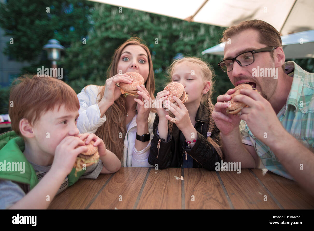 hungry family eating hamburgers, sitting at a table in a fast food ...