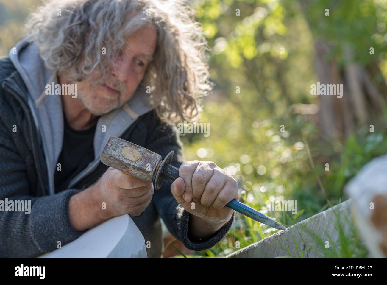 Senior sculptor carving into stone working outside on a sunny day Stock ...