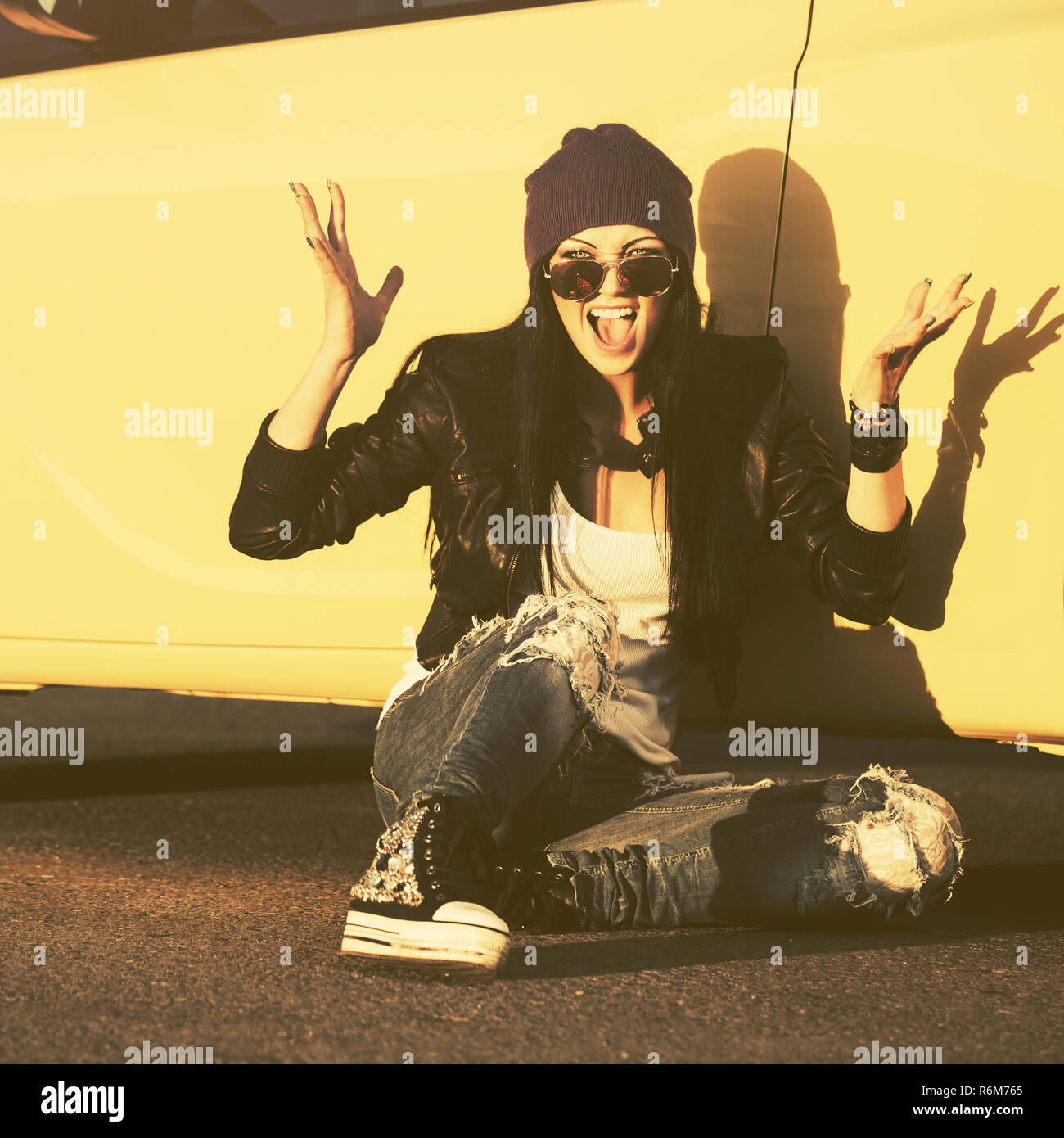 Angry fashion hipster woman in black leather jacket sitting on sidewalk ...