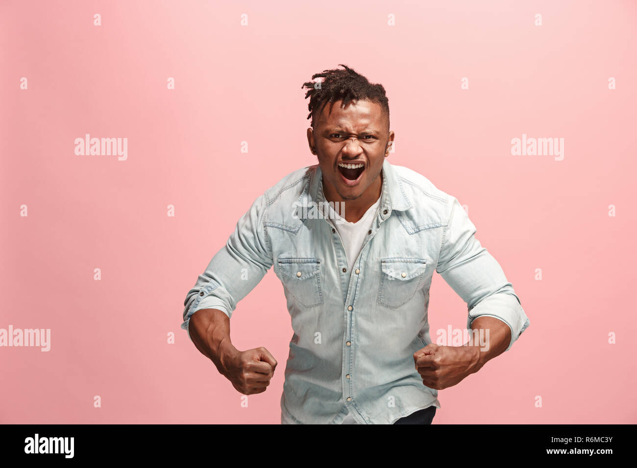 The young emotional angry afro man screaming on pink studio background ...