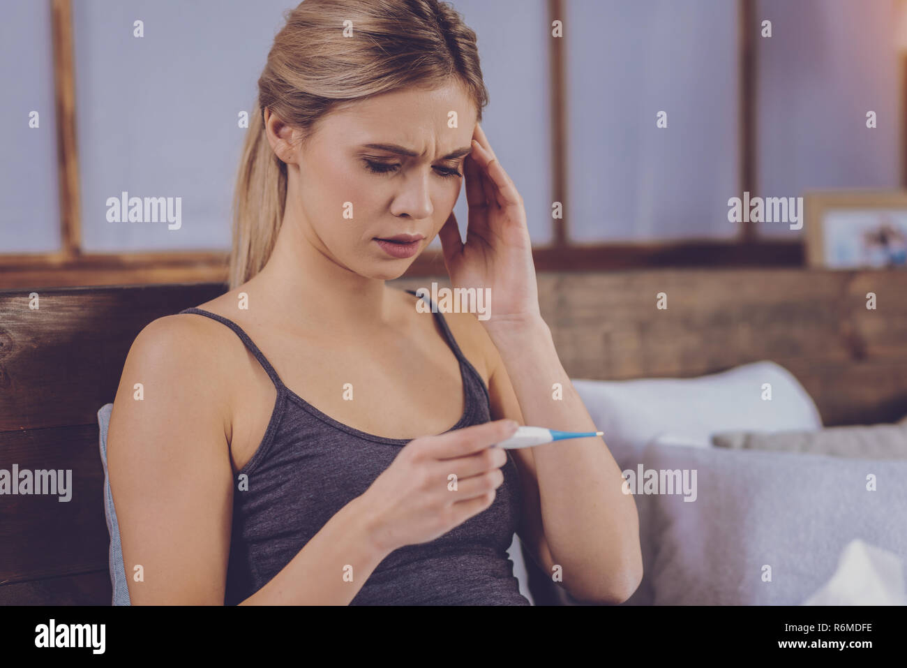 Fair-haired young woman having fever and checking thermometer Stock ...
