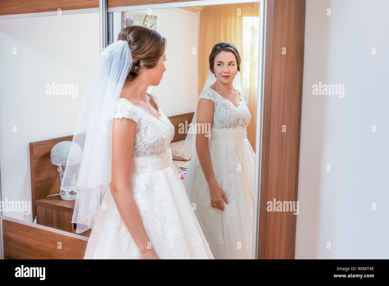 Bride in white dress looking in the mirror Stock Photo - Alamy