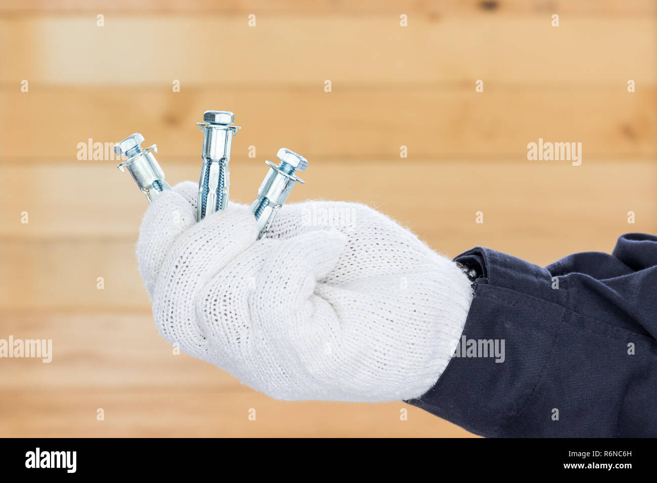 Hand in glove holding metal anchor bolt Stock Photo - Alamy