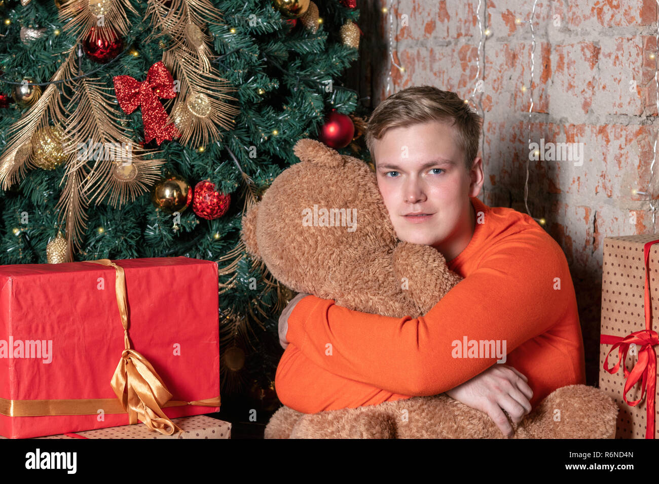 Handsome guy hugs the bear sitting under the tree surrounded by gifts ...