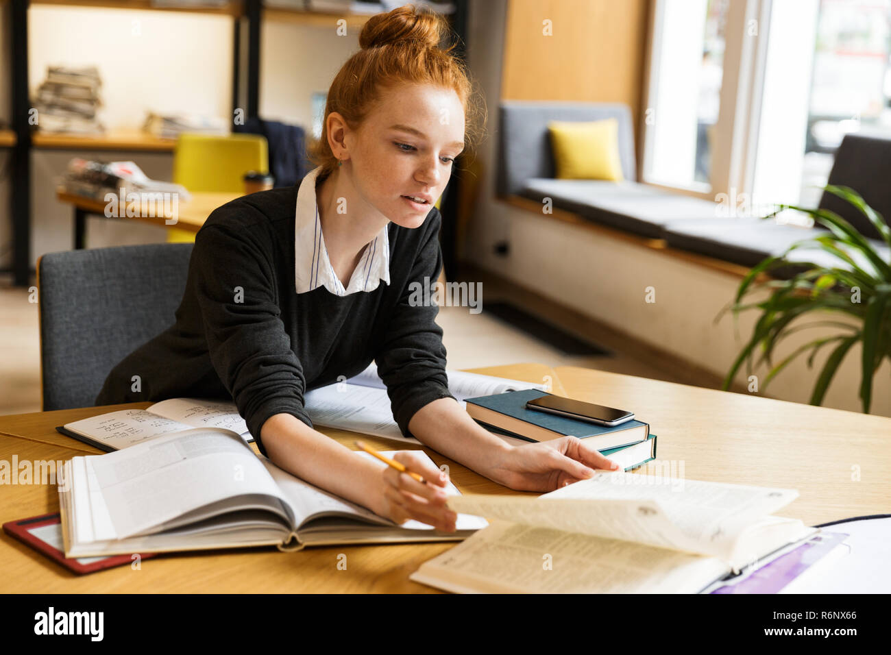 Smart red haired teenage girl studying at the table in library Stock ...