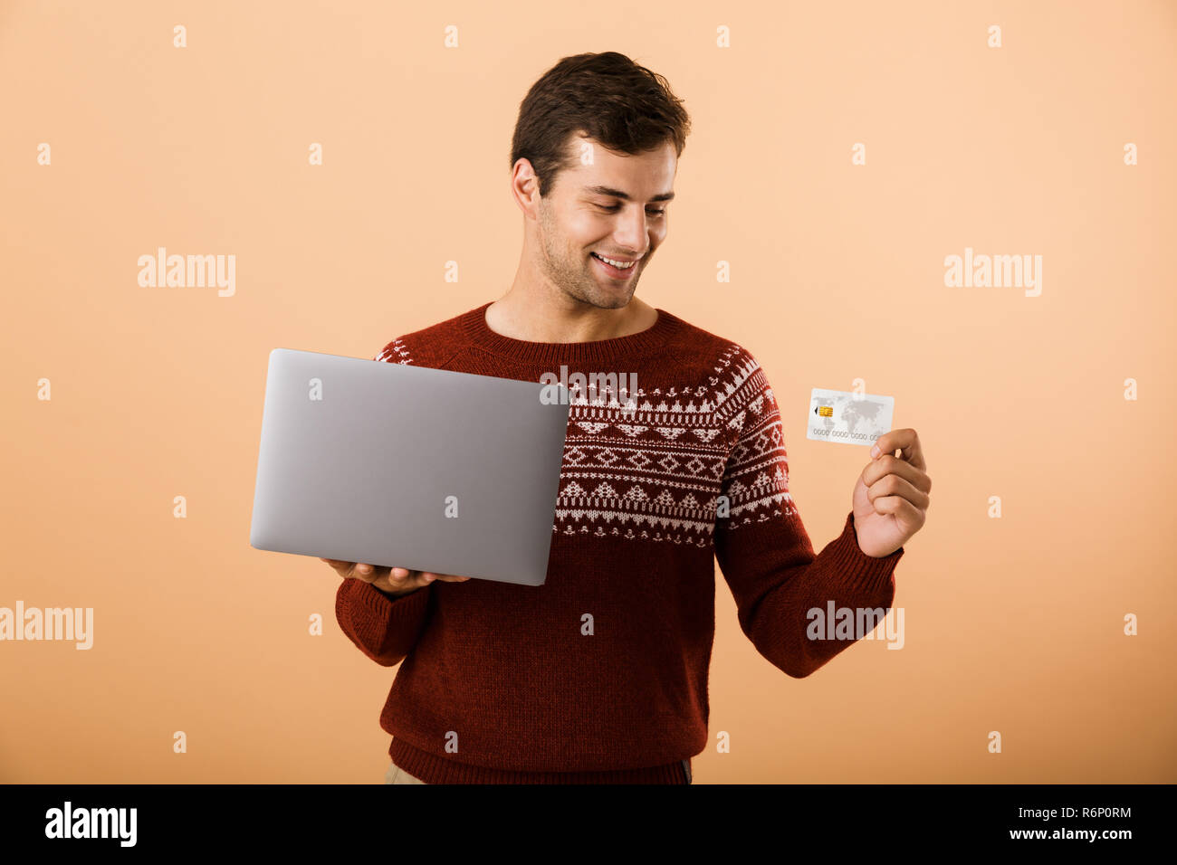 Portrait a smiling young man dressed in sweater isolated over beige ...
