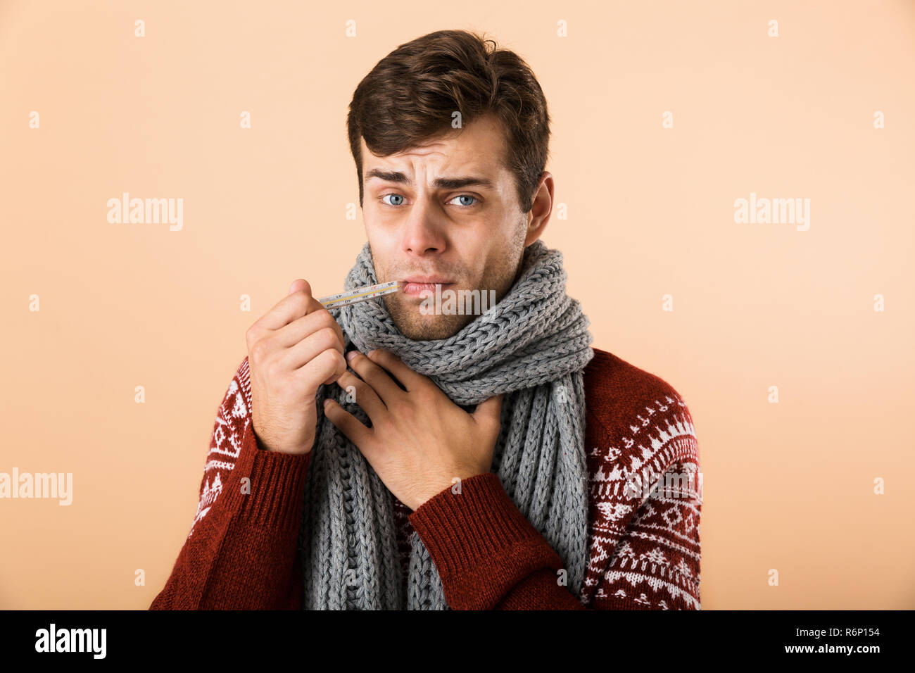 Portrait of a sick young man dressed in sweater and scarf isolated over ...