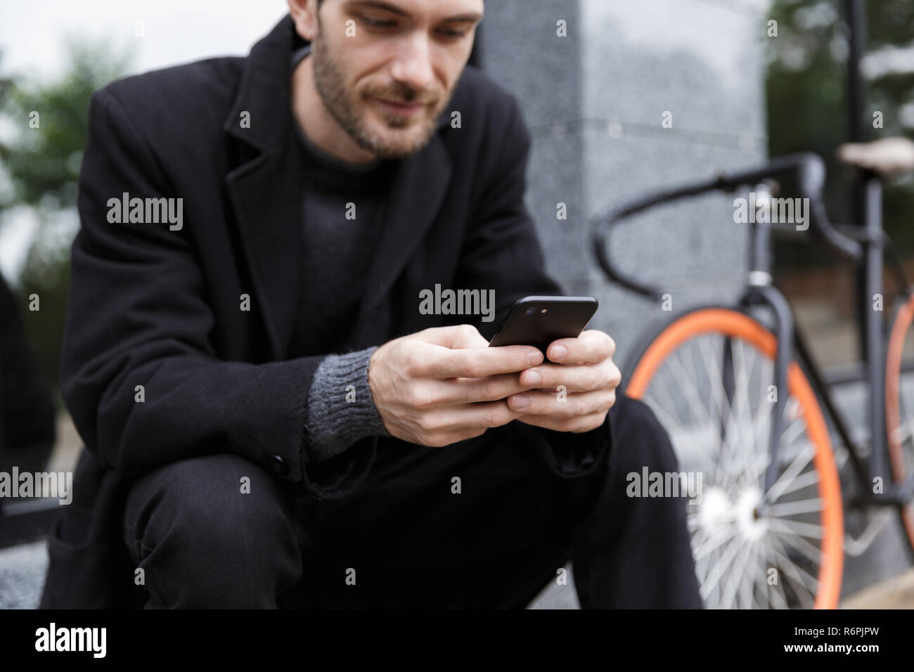 Photo of young man 20s using mobile phone while sitting outdoor with ...