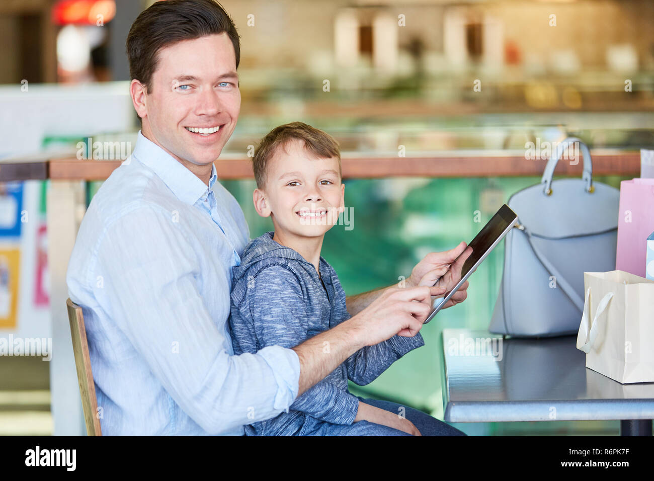 Father and son using tablet computer while shopping in shopping mall ...