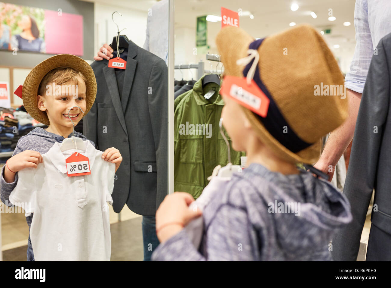 Boy at fitting in front of the mirror in fashion store during sale ...