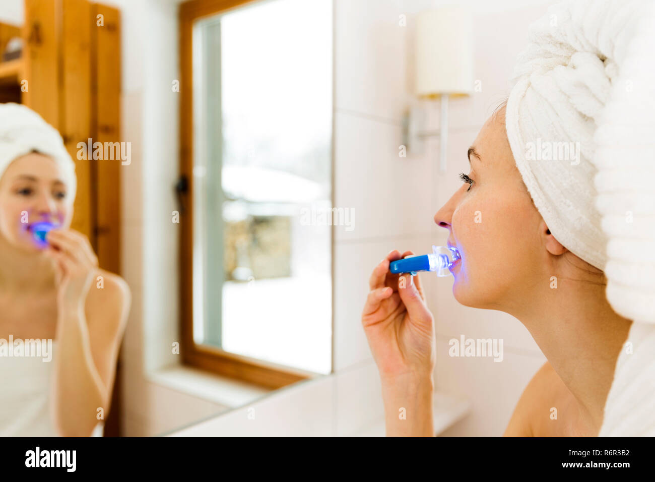 Woman is whitening teeth with special toothpaste and LED light at home ...
