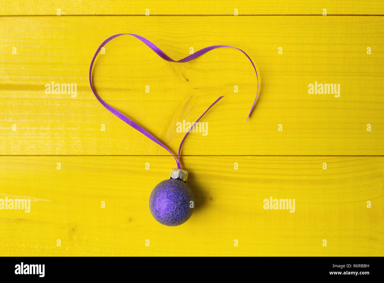 Blue Christmas ball with long ribbon over wooden yellow background ...