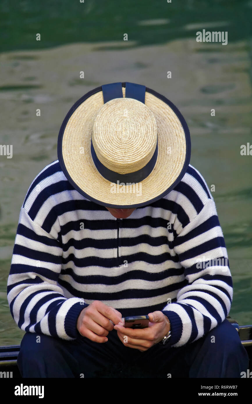 A gondolier in his traditional costume sits while checking his ...