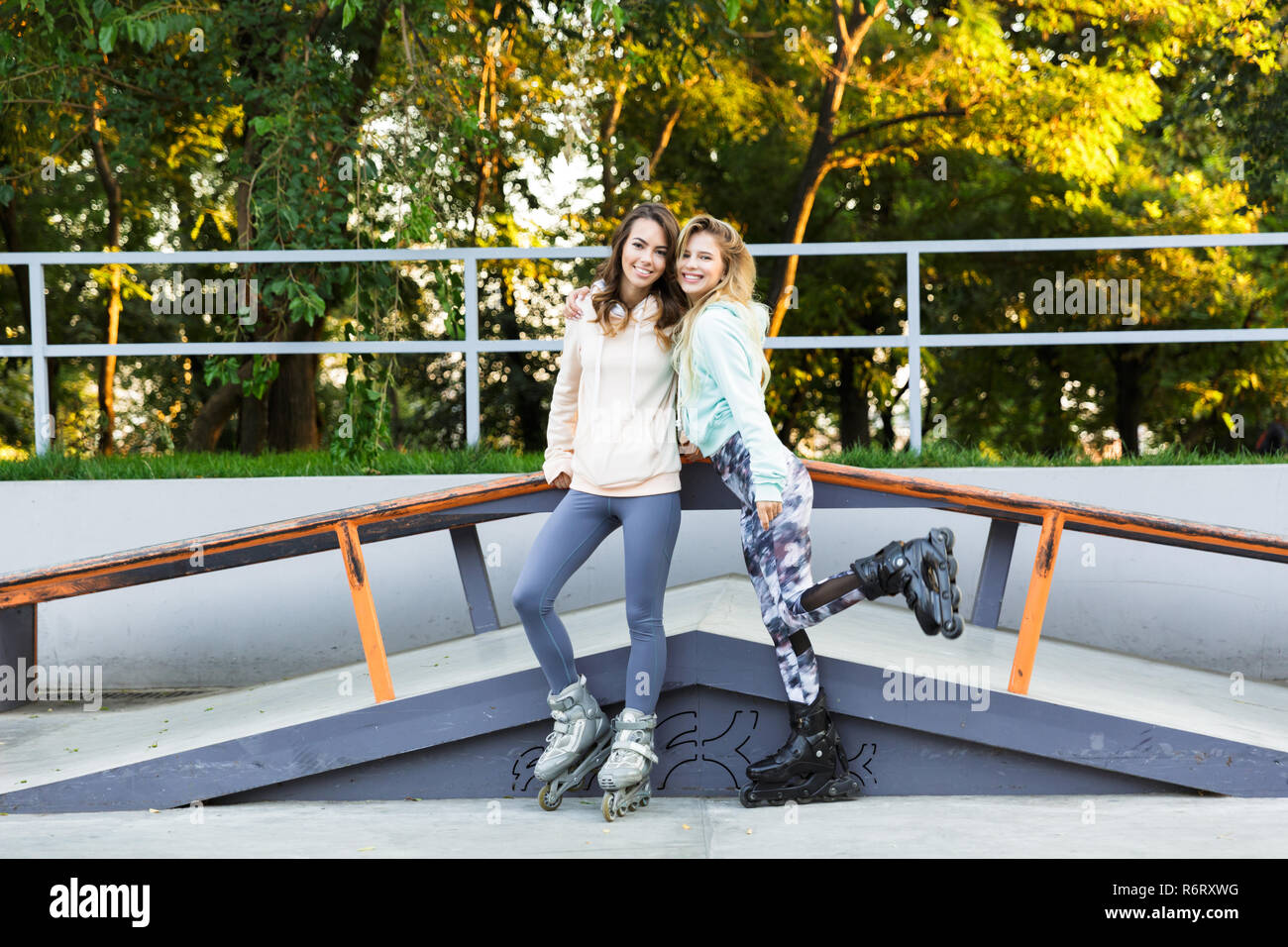 Image of happy two girls friends sisters on rollers in park outdoors ...