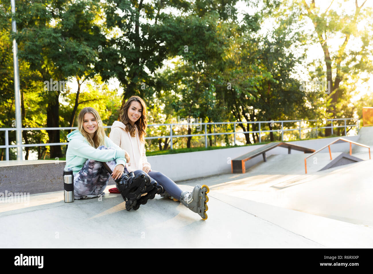 Image of happy two girls friends sisters on rollers sitting in park ...