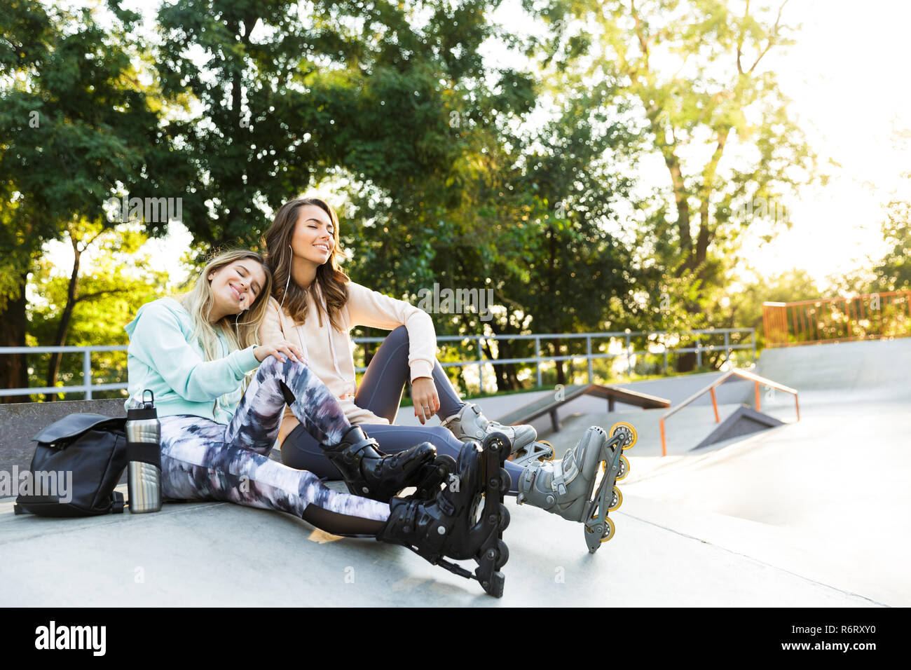Image of happy two girls friends sisters on rollers sitting in park ...