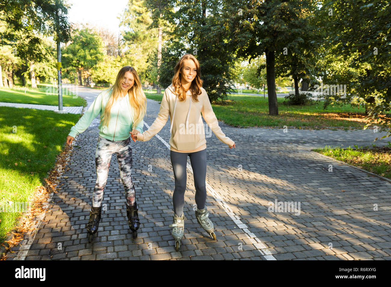 Two cheerful young girls on on roller skates spending time at the park ...