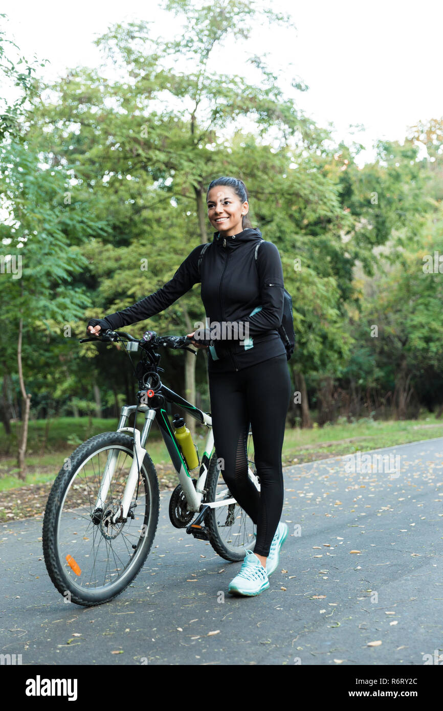 Image of a beautiful woman walking on bicycle in the park outdoors ...