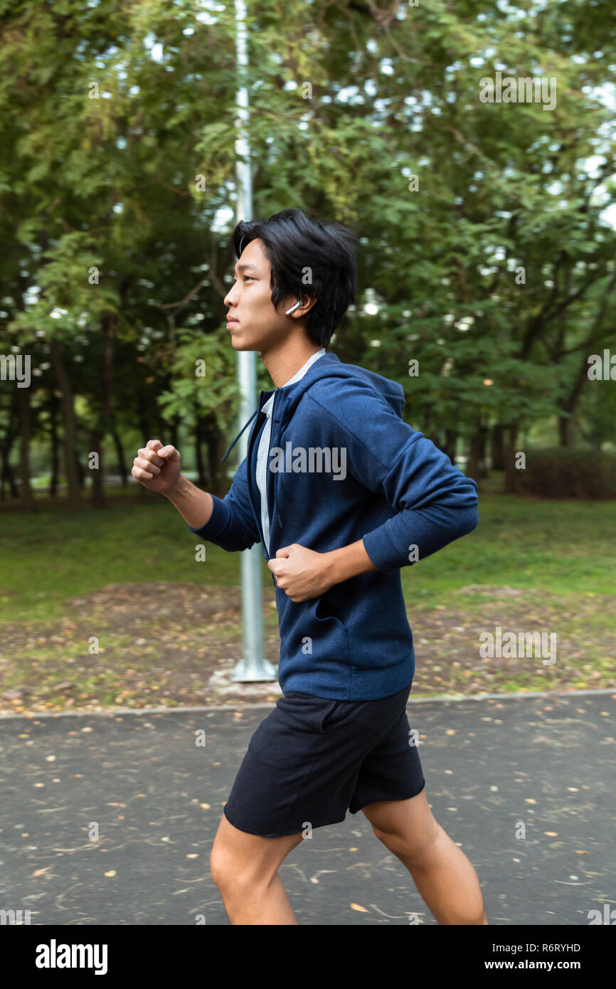 Strong young asian man jogging at the park, listening to music with ...