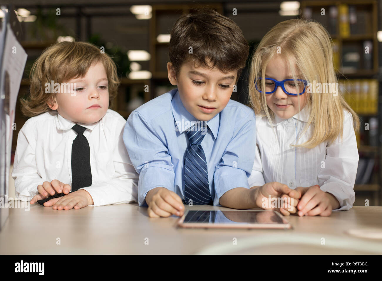 Three little children on business meeting sit at the table in the ...