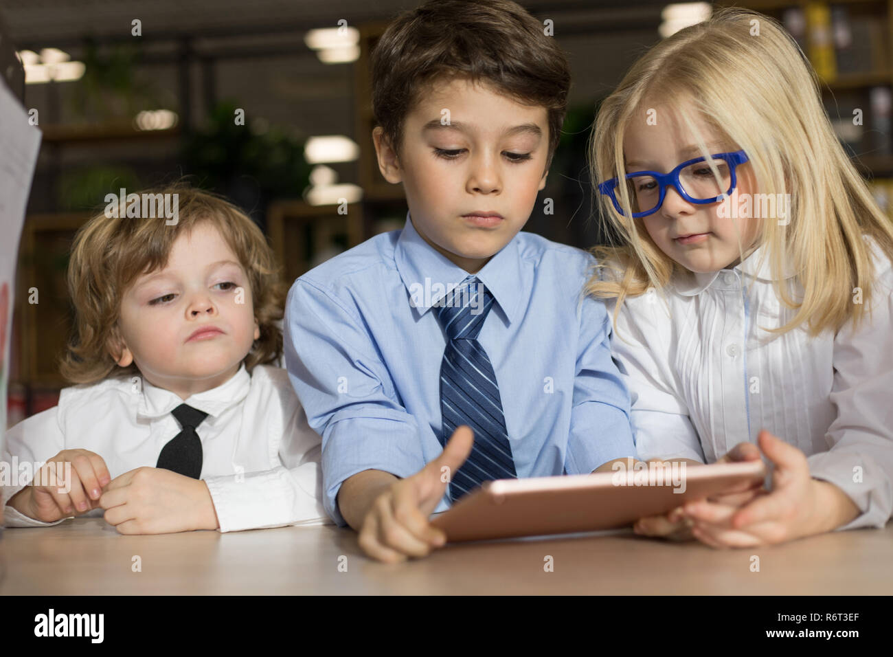 Three little children on business meeting sit at the table in the ...