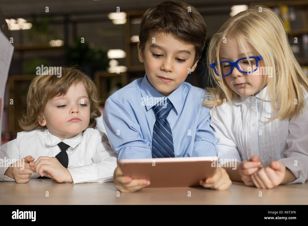 Three little children on business meeting sit at the table in the ...