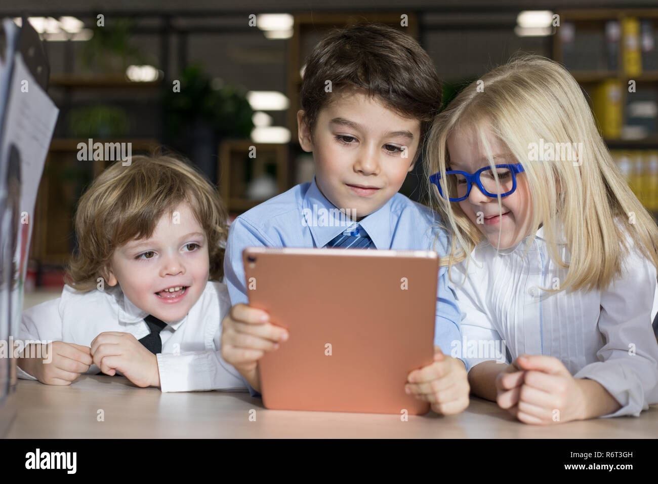Three little children on business meeting sit at the table in the ...