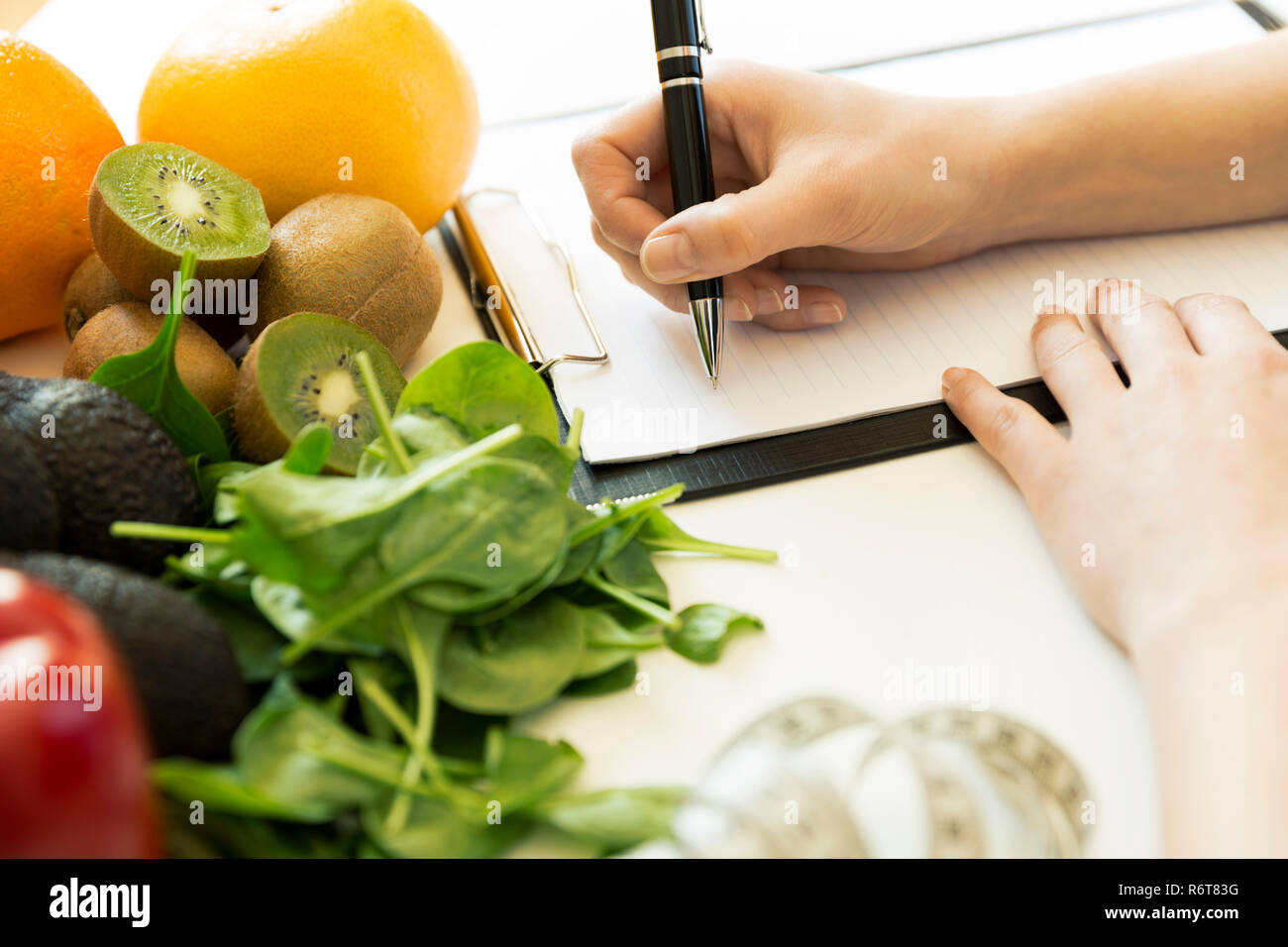 Nutritionist woman writing diet plan on table full of fruits and ...