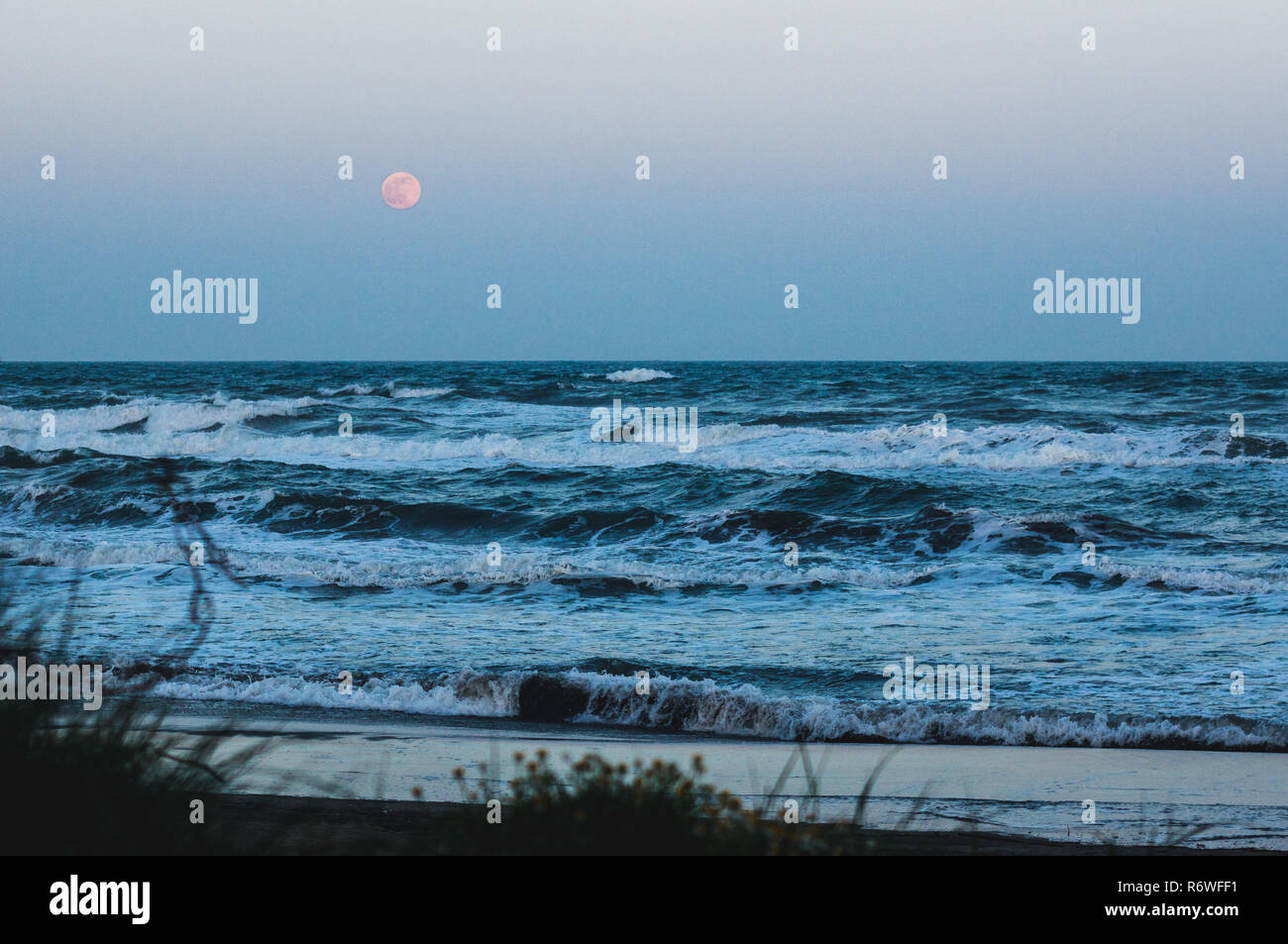 wild sea with full moon in background, focus on big waves at the beach ...
