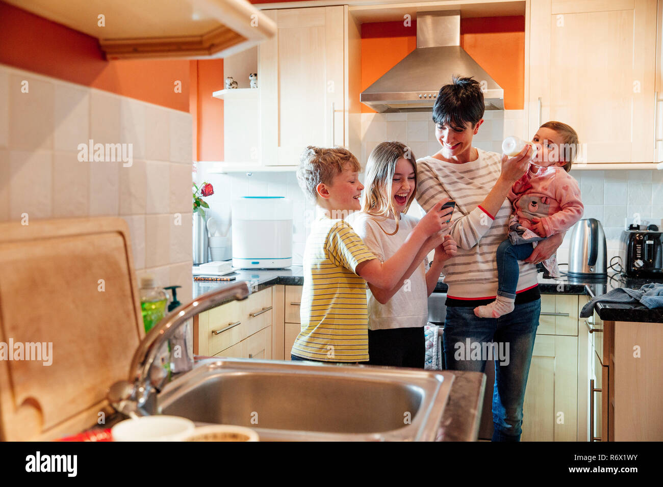 Multitasking Mum with her Children at home Stock Photo - Alamy