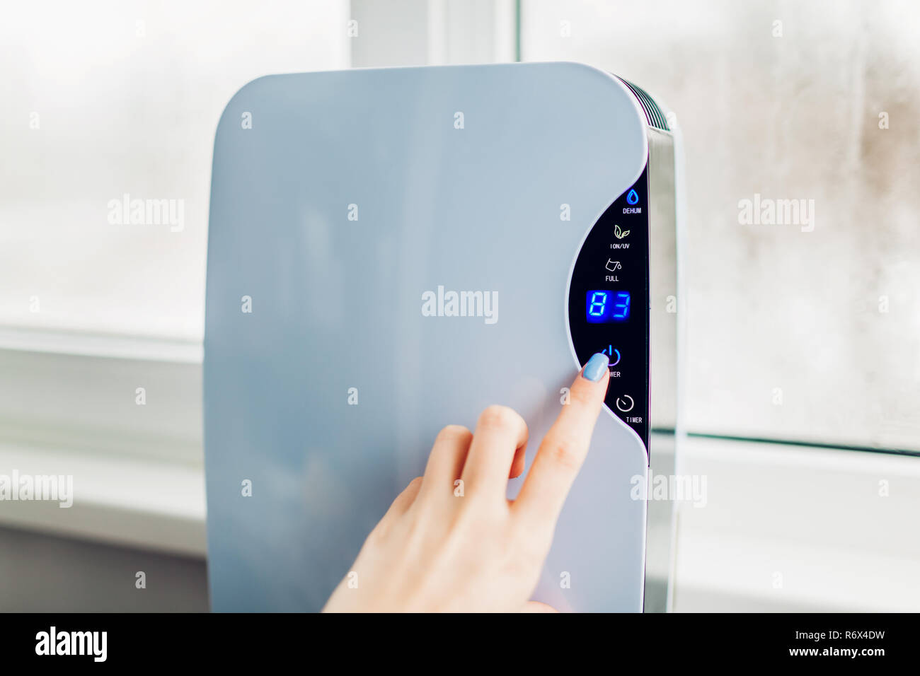 Woman turns dehumidifier on using touch panel by wet window. Humidity ...