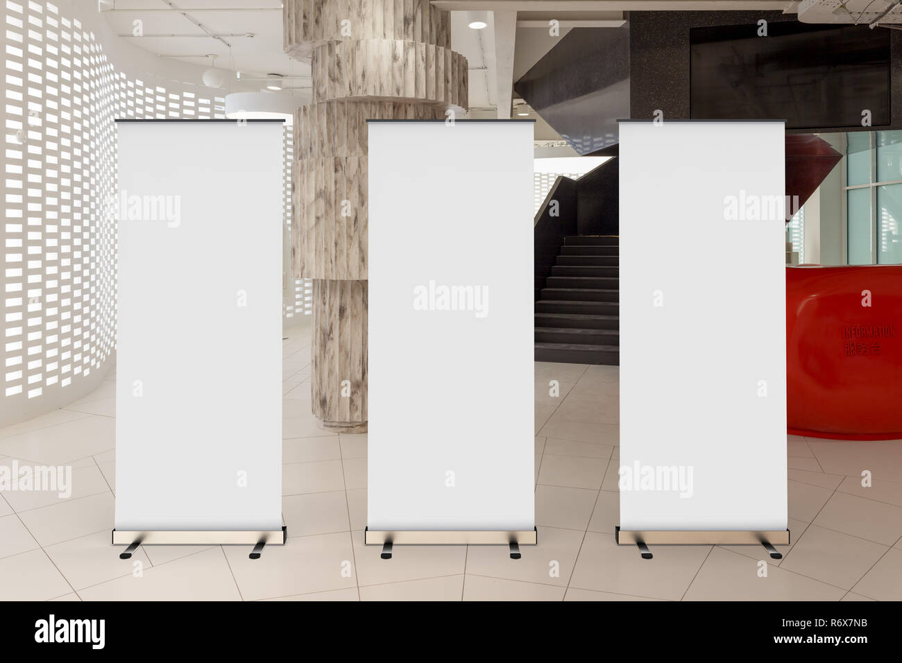 Three blank roll up banner stand in office interior with reception desk ...