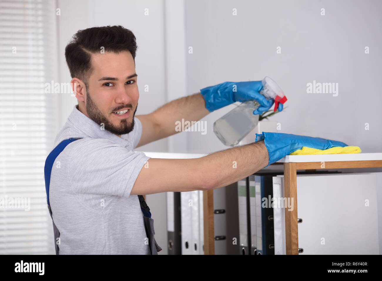 Male Cleaner Cleaning Shelf At Workplace Stock Photo - Alamy