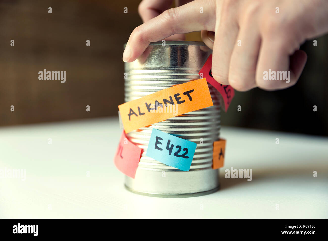 Woman's hand opening canned food with paper notes naming food additives ...