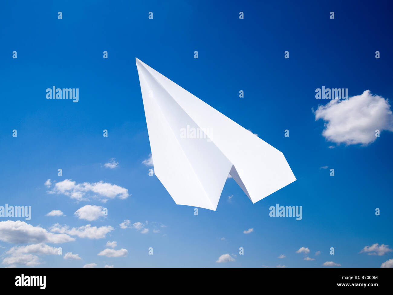 White paper airplane in a blue sky with clouds. The message symbol in ...