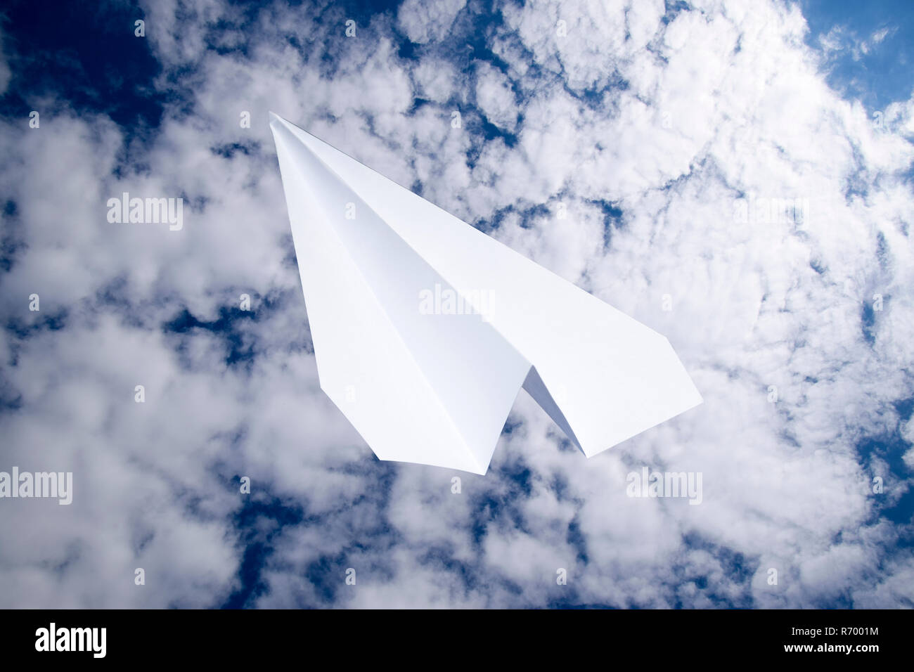 White paper airplane in a blue sky with clouds. The message symbol in ...