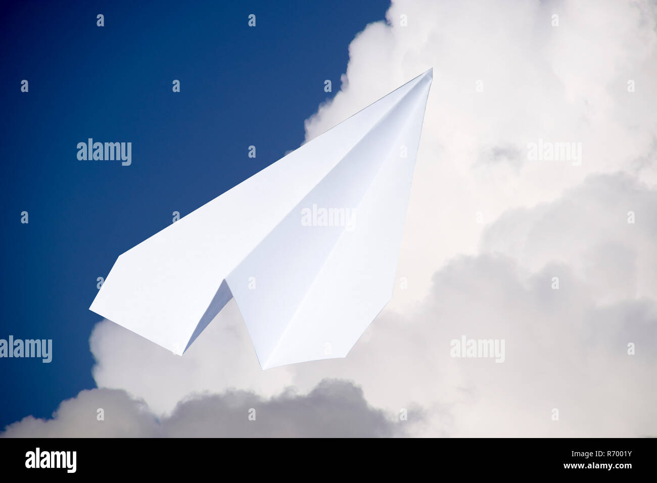 White paper airplane in a blue sky with clouds. The message symbol in ...