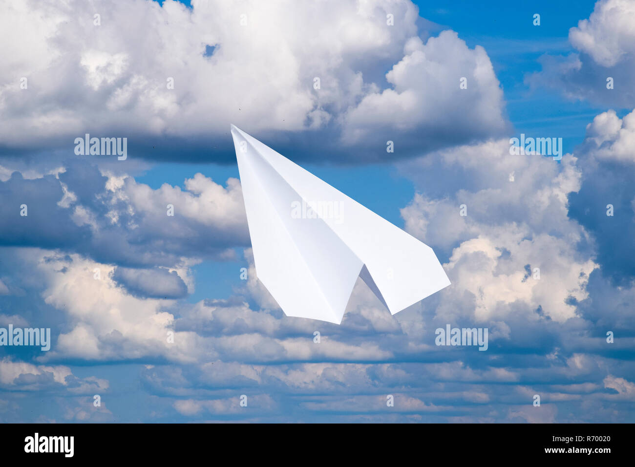 White paper airplane in a blue sky with clouds. The message symbol in ...