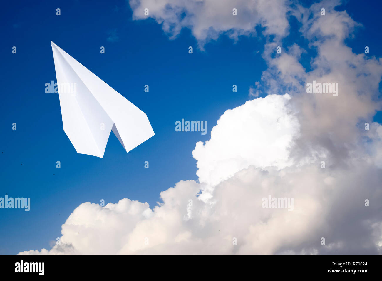 White paper airplane in a blue sky with clouds. The message symbol in ...