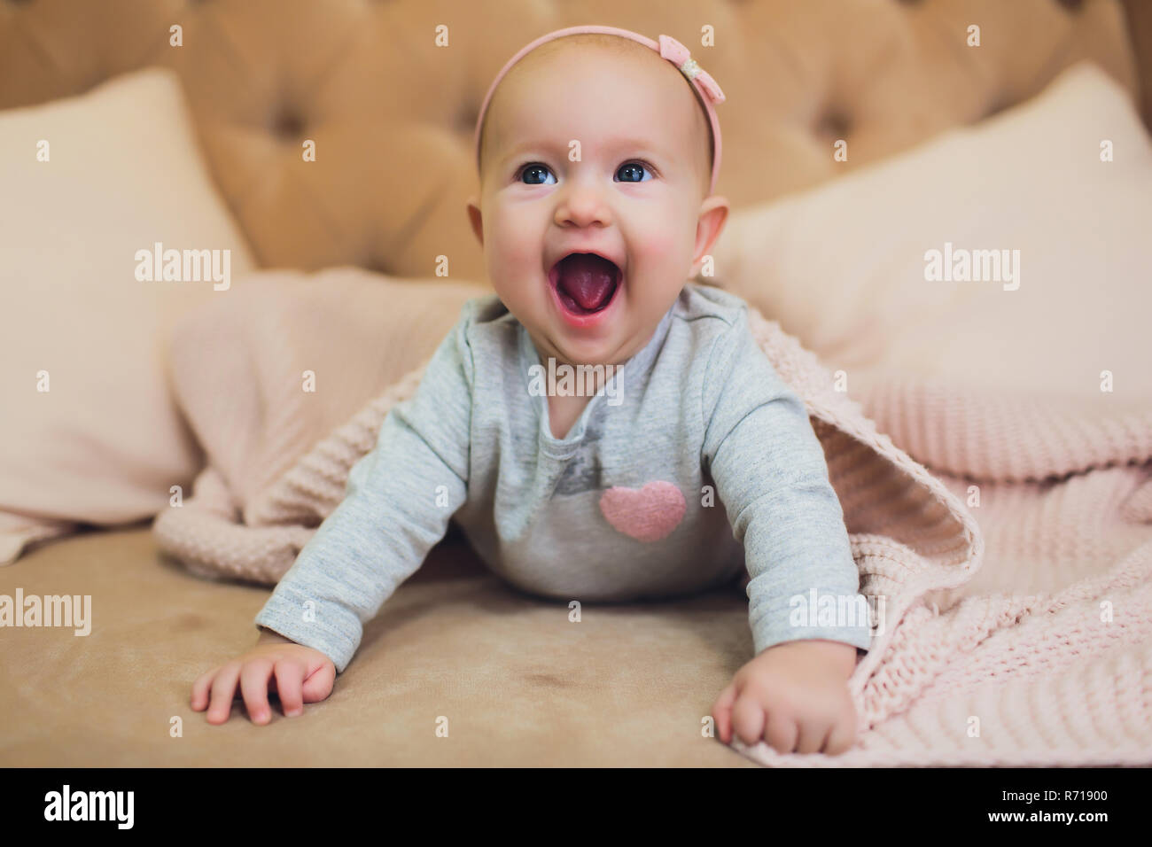 Sweet adorable baby girl lying on a couch looking towards camera. 6-7 ...