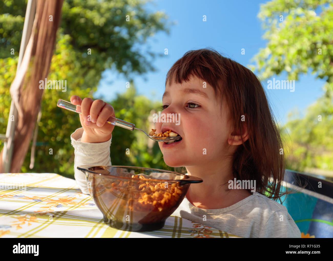 Cute little girl eat flakes with milk . Summer sunny day in the garden ...