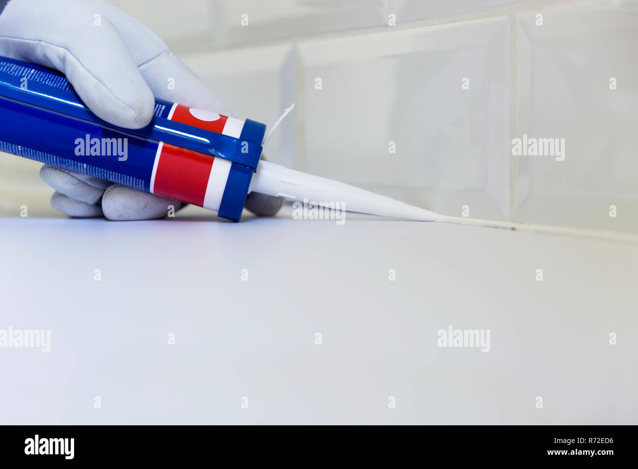 Plumber applying silicone sealant to the countertop and ceramic tile ...