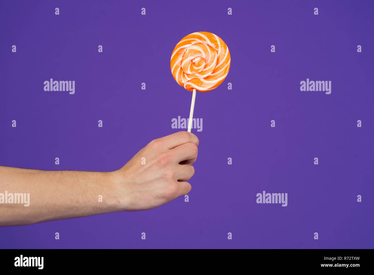 Lollipop in hand on violet background. Candy on stick on purple ...