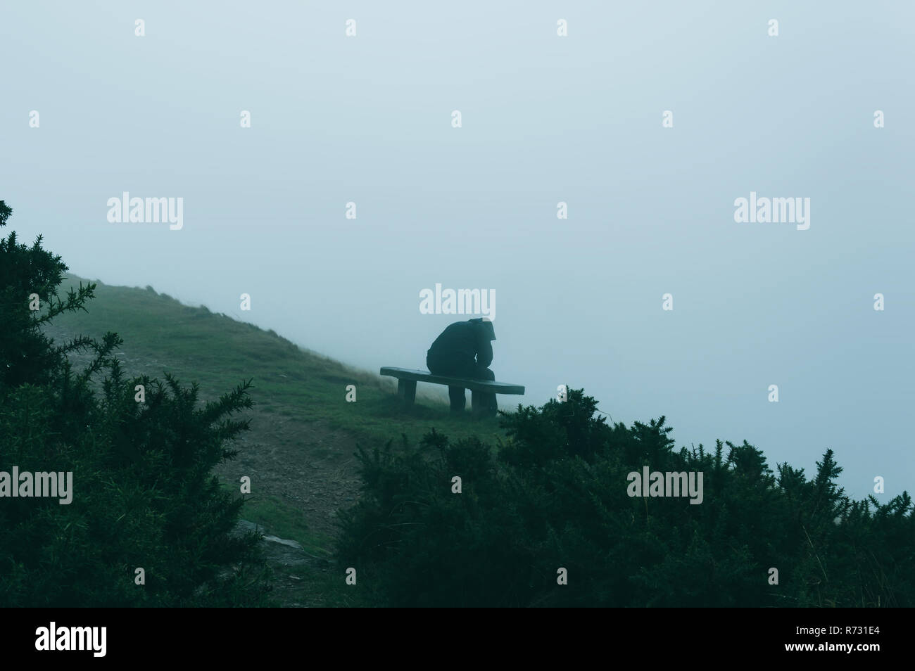 A sad hooded man sitting on a bench looking away and down from the ...