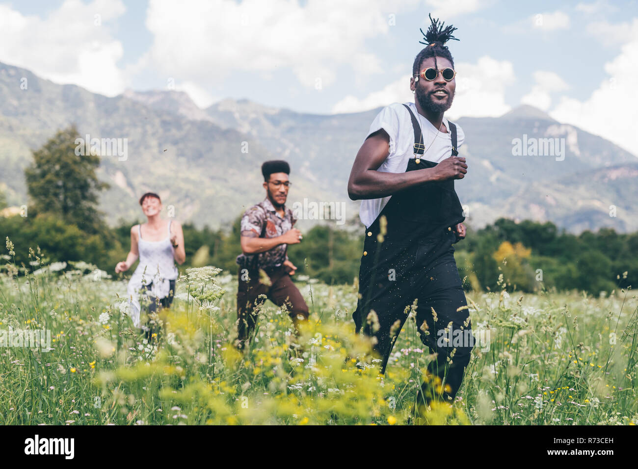 Three adult friends racing through wildflower meadow, Primaluna ...