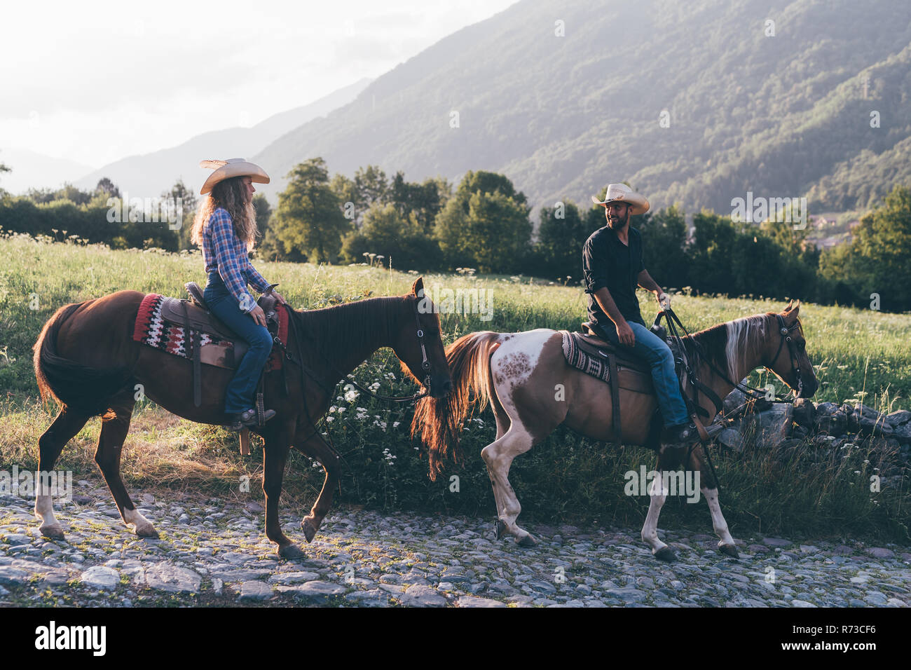 Cowgirl and cowboy riding horses on rural cobbled road, Primaluna ...